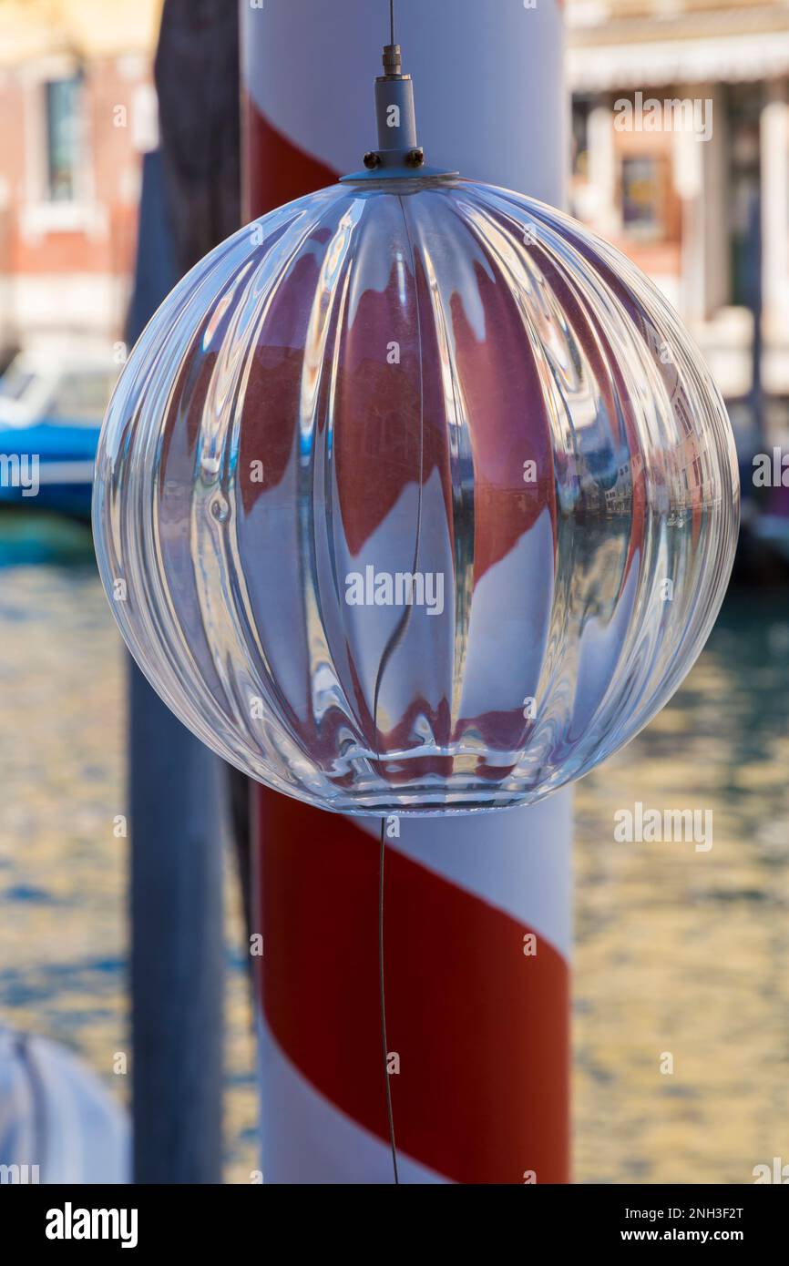 Close up of Murano glass light with reflections of red and white striped mooring pole post ...