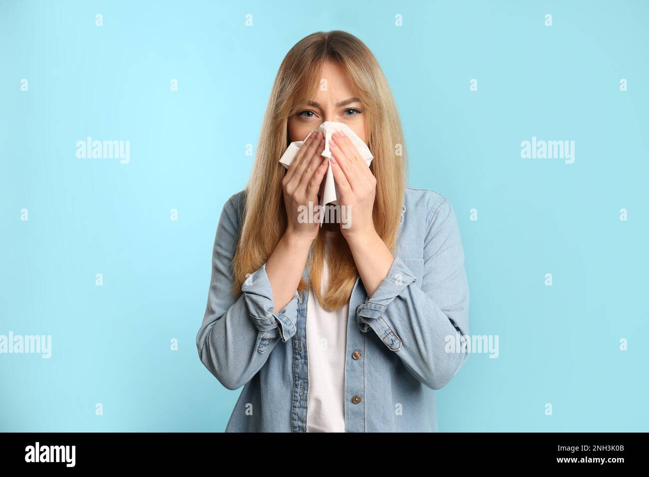 Young woman with tissue suffering from runny nose on light blue ...