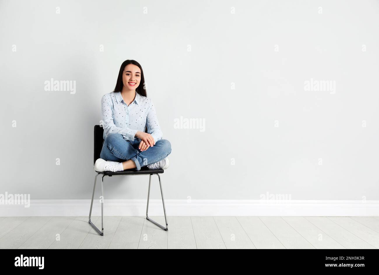 Young woman sitting on chair near white wall in office, space for text ...