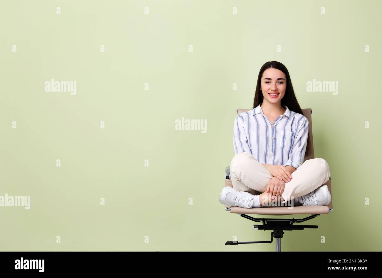 Young woman sitting in office chair on green background, space for text ...
