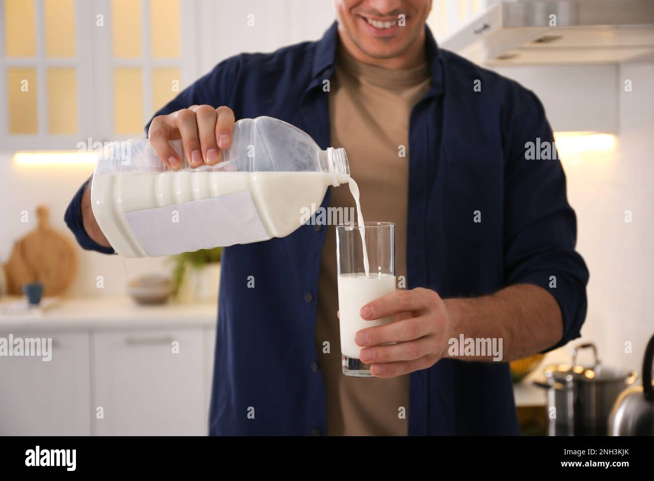 Man pouring milk from gallon bottle into glass in kitchen, closeup ...
