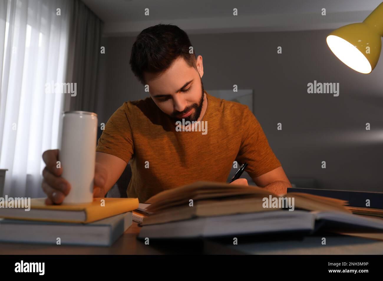 Tired young man with energy drink studying at home Stock Photo - Alamy