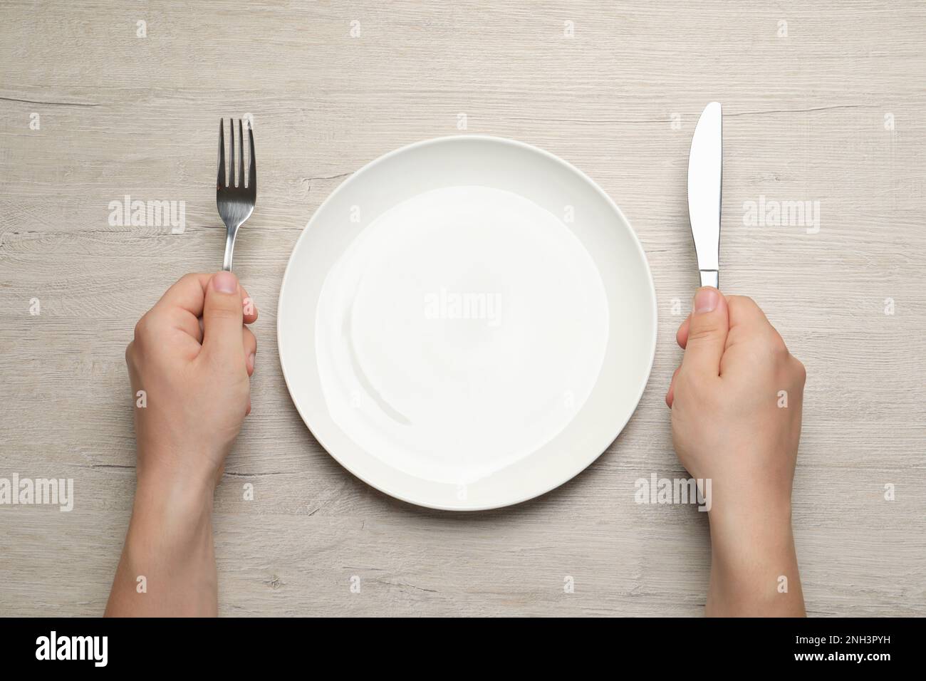 Top view of man with cutlery and empty plate at wooden table, closeup ...