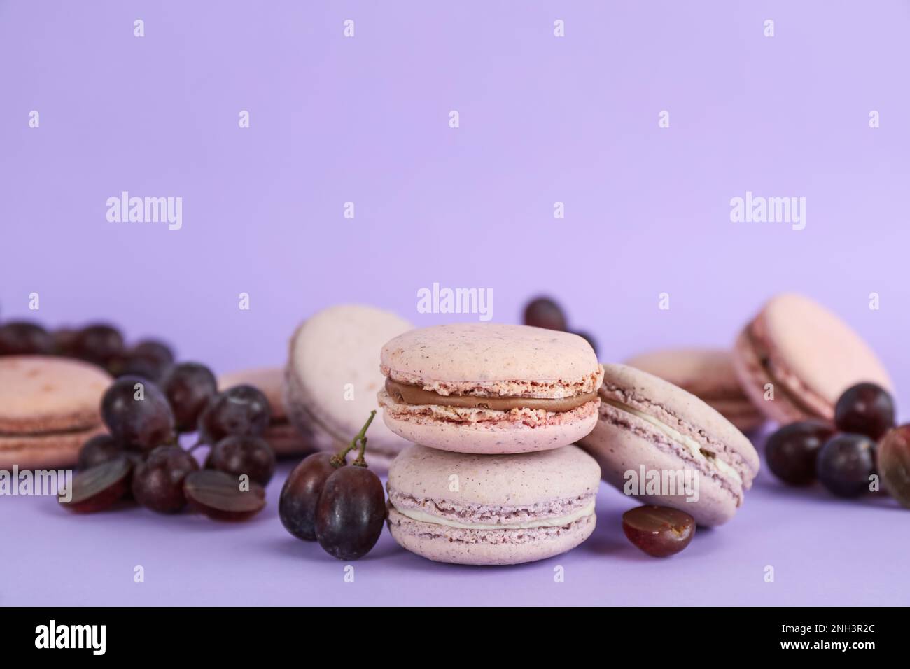 Delicious macarons and grapes on violet background, space for text ...
