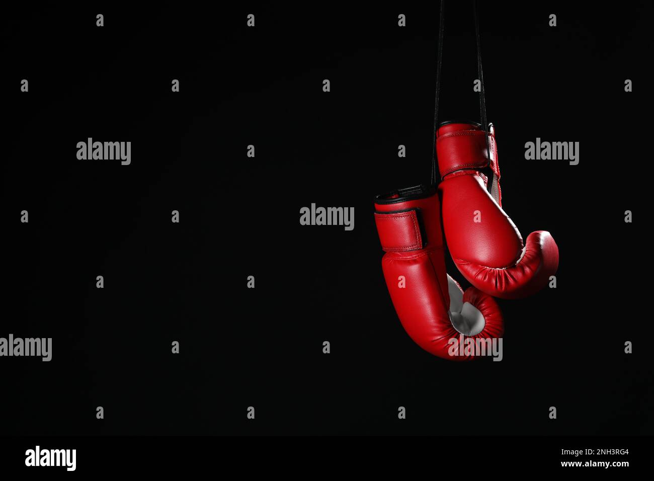 Pair of red boxing gloves hanging on black background, space for text ...