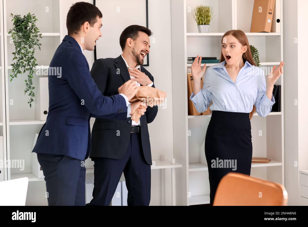 Young men with paper bag playing a prank on their colleague in office ...