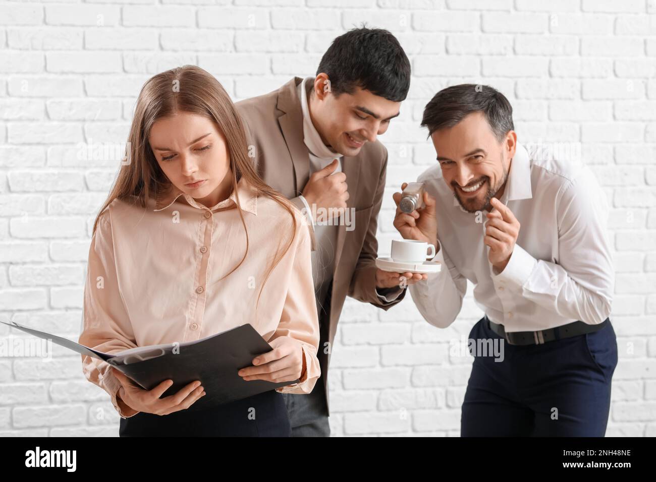 Young men sprinkling pepper in their colleague's cup of coffee on white ...