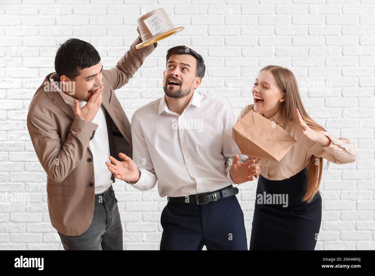Business people playing a prank on their colleague against white brick ...