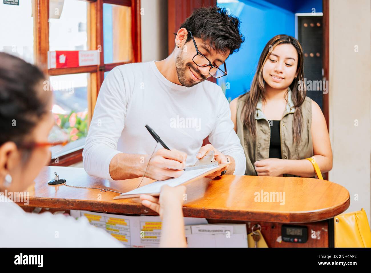 Couple signing in at a hotel reception. Young couple signing documents ...