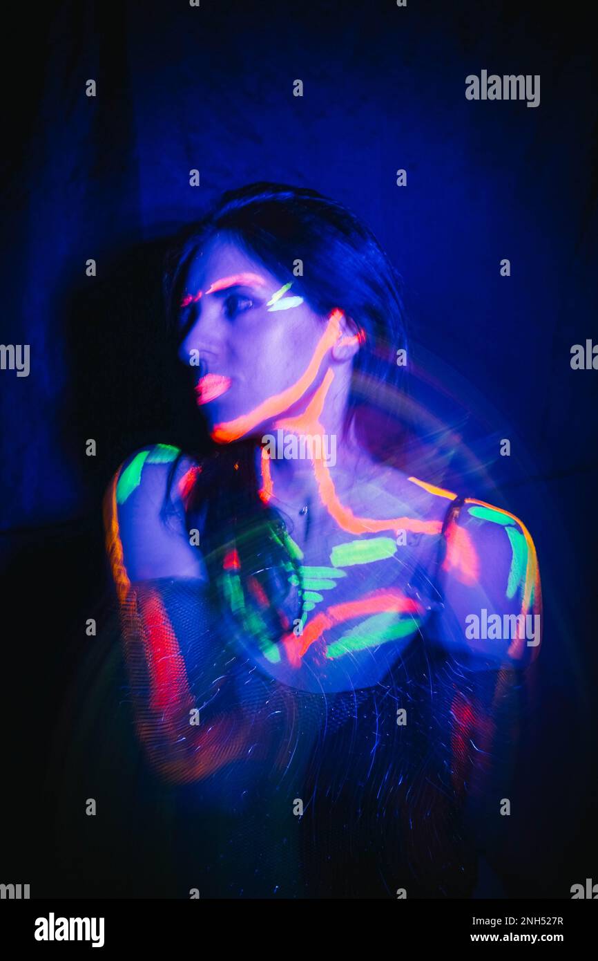 A beautiful young girl with makeup from ultraviolet paints smokes ...