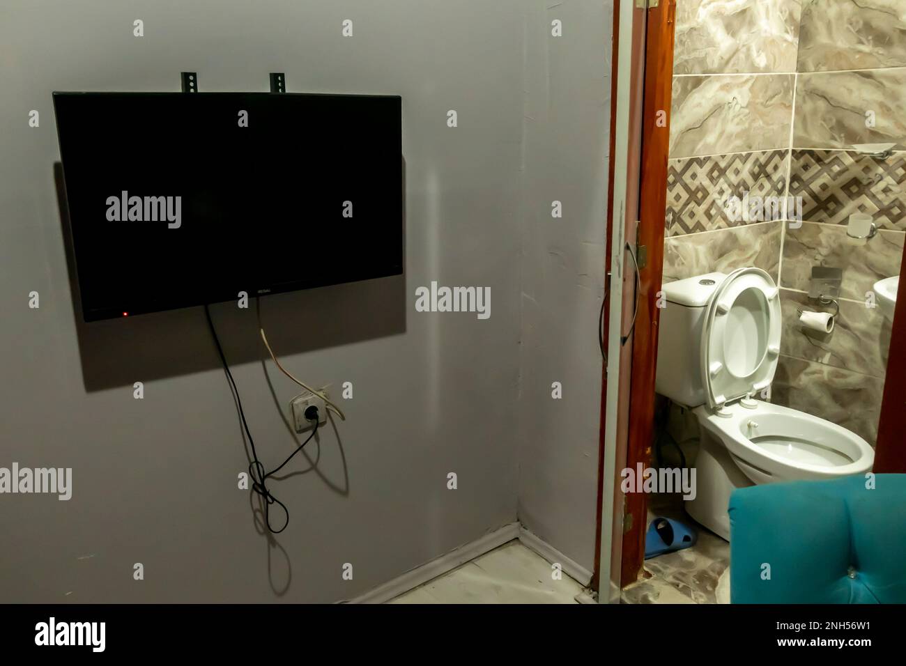 Simple seedy weird hotel room with TV on a wall next to the toilet ...