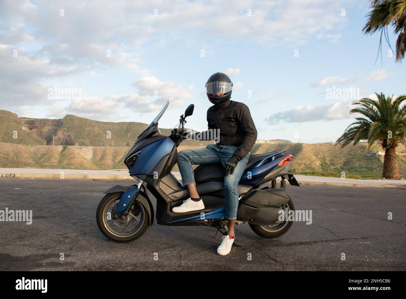 Full length of an African American biker sitting on his scooter. Arid ...