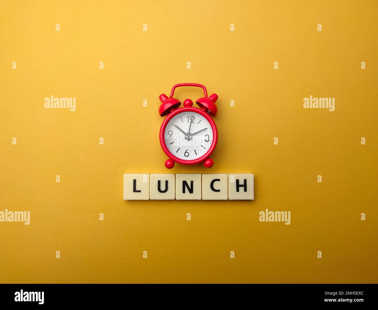 Red alarm clock with word LUNCH on a yellow background Stock Photo - Alamy
