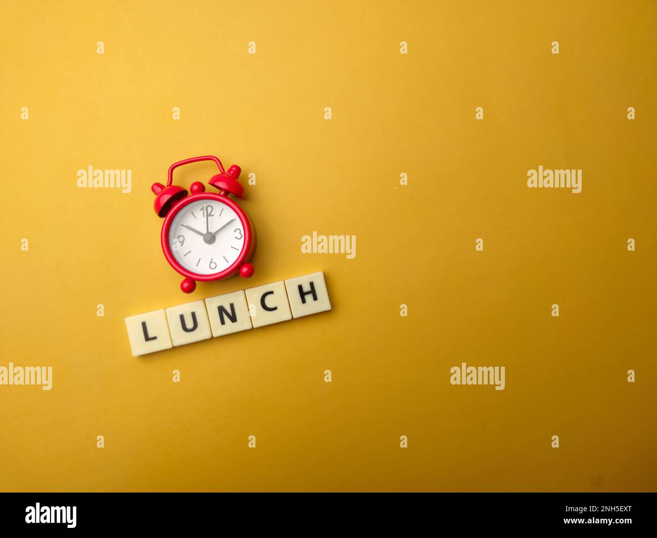 Red alarm clock with word LUNCH on a yellow background Stock Photo - Alamy