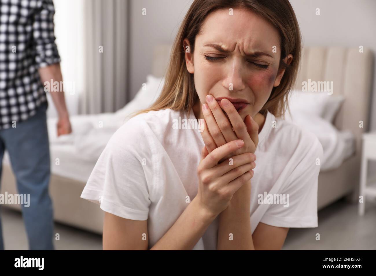 Scared woman with injuries and abuser in bedroom. Domestic violence ...