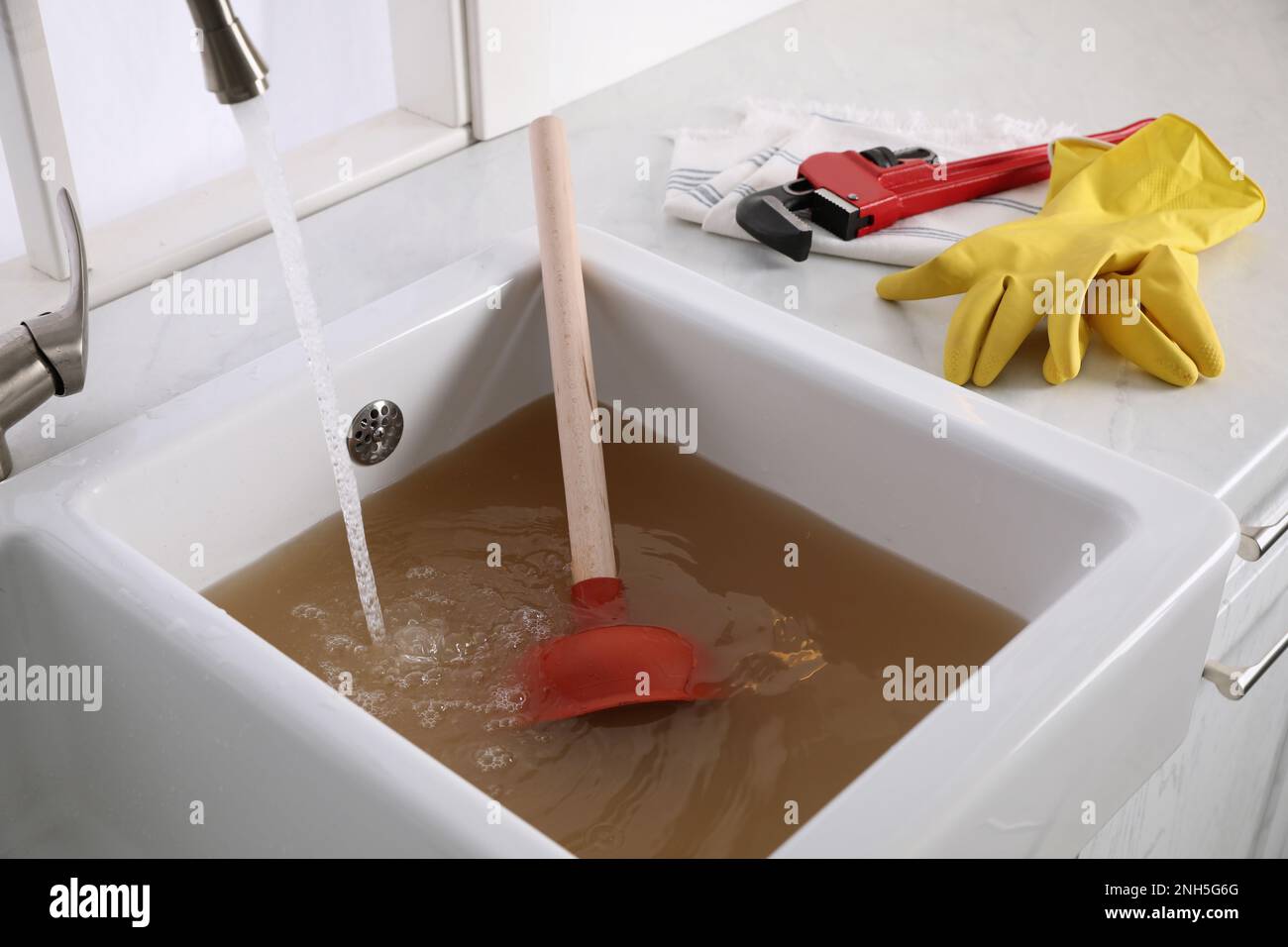 Kitchen counter with clogged sink, plunger and plumber's accessories ...