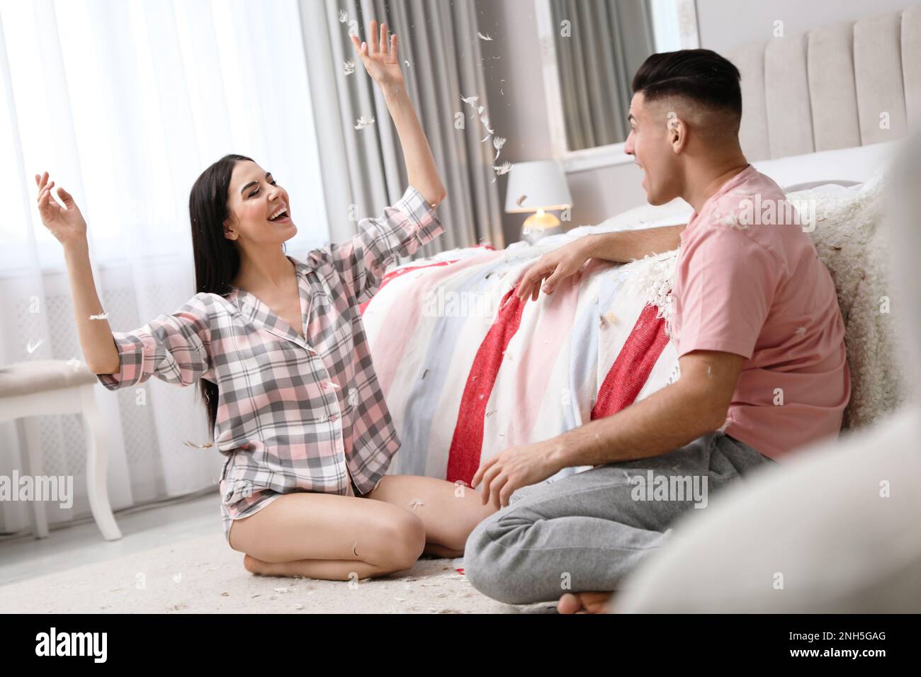 Happy couple having fun with flying feathers after pillow fight in ...