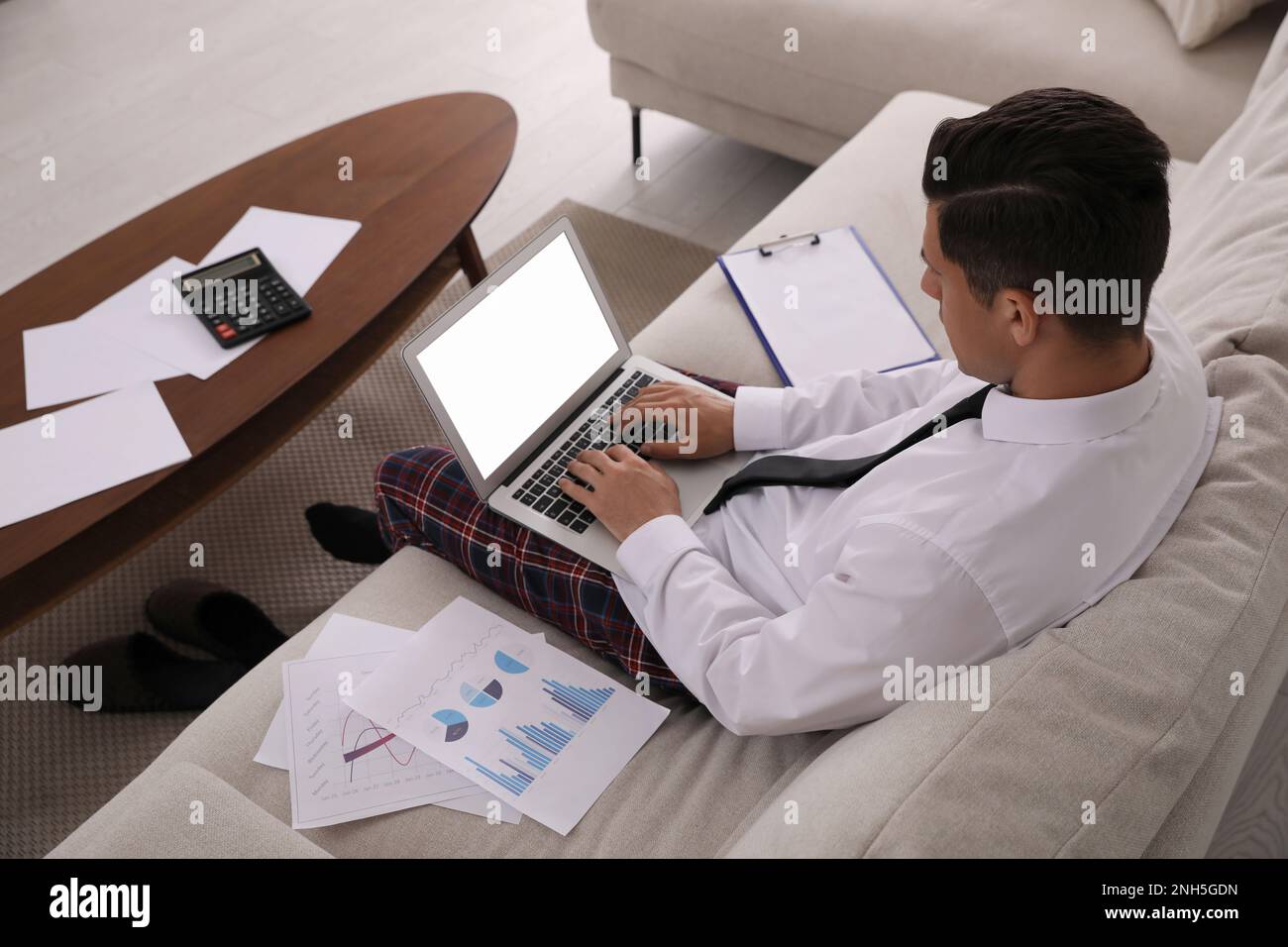 Man in shirt and pajama pants working on laptop indoors. Stay at home ...