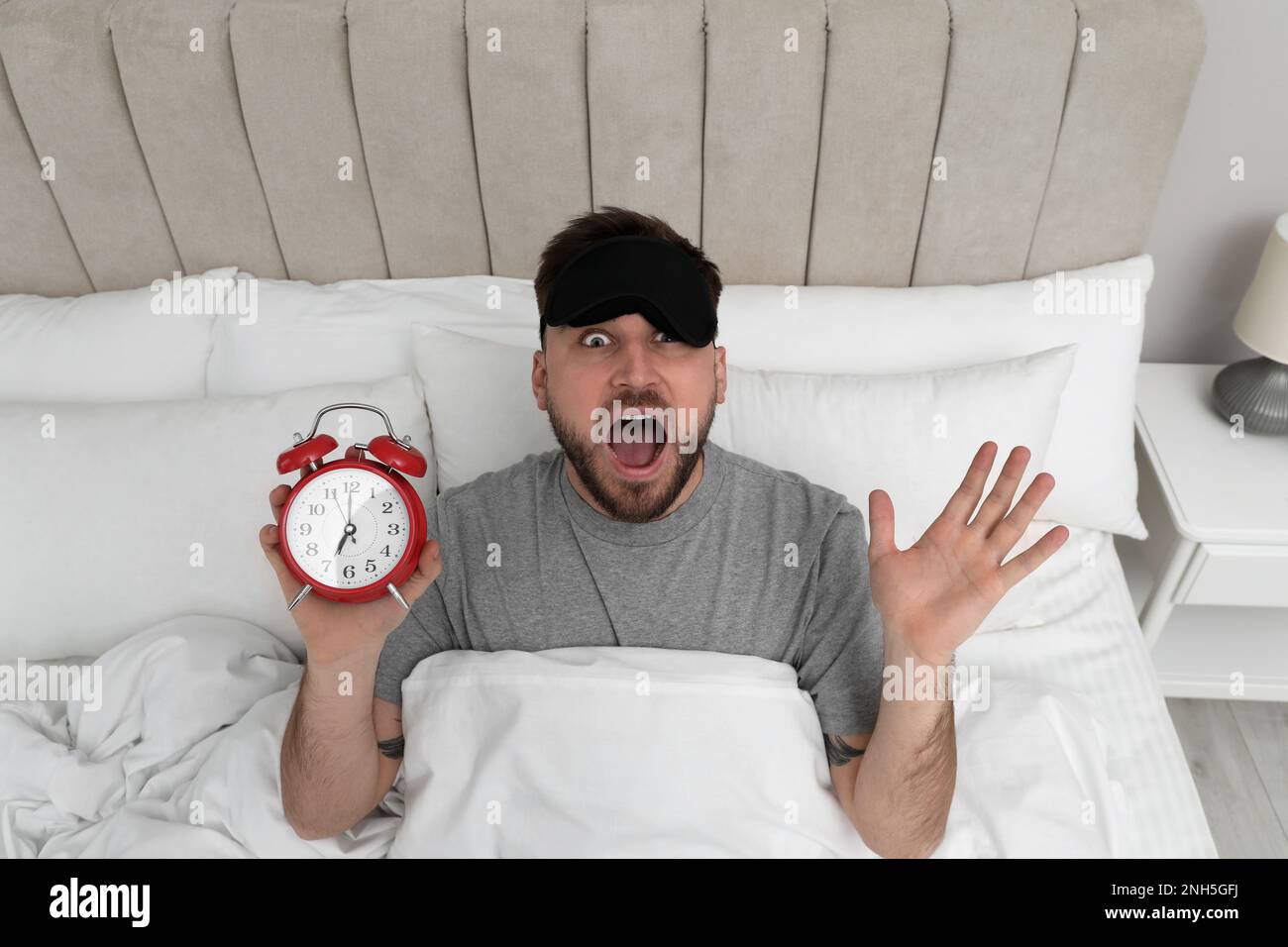 Emotional overslept man with alarm clock in bed, above view. Being late ...