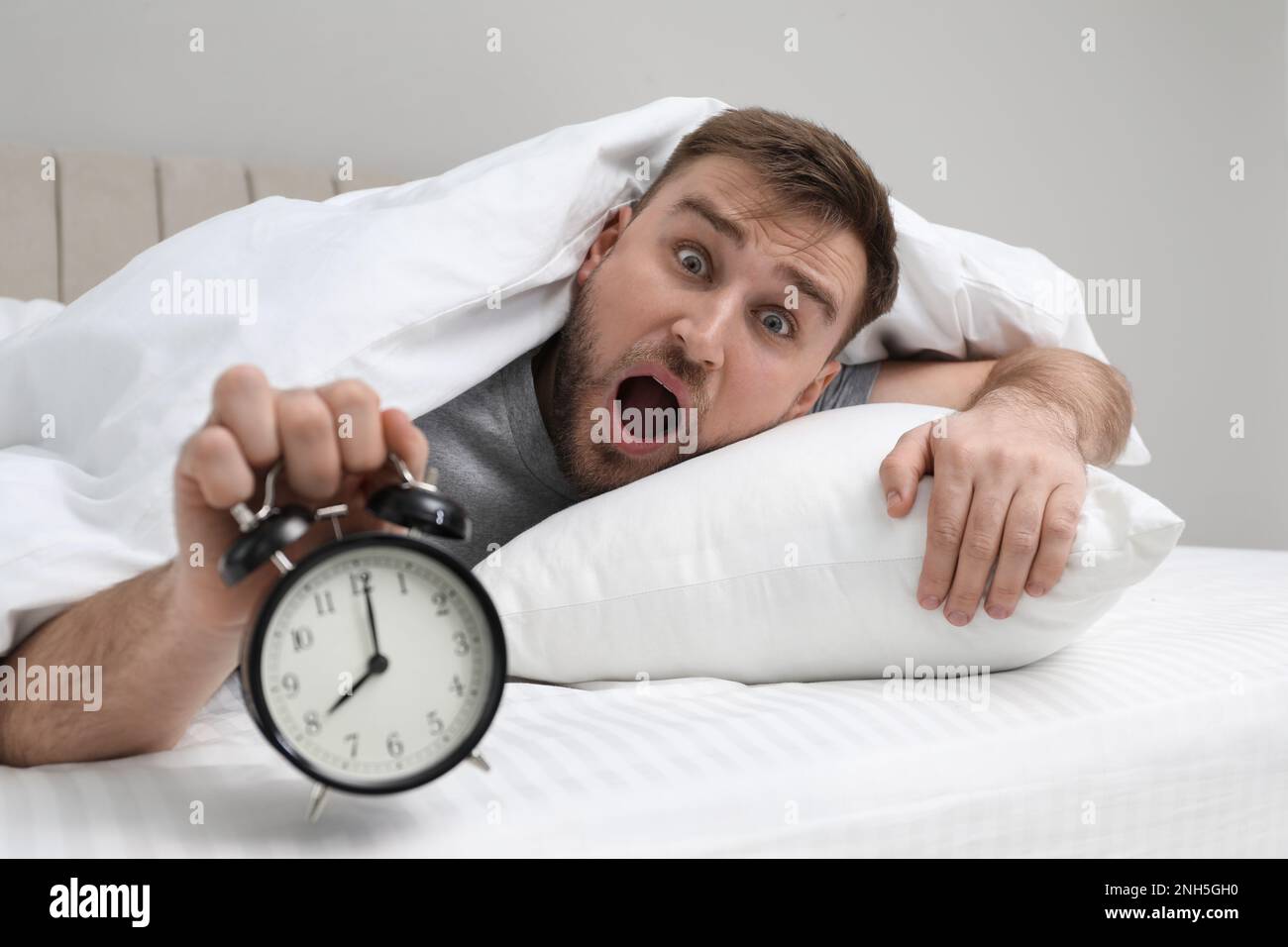 Emotional overslept man with alarm clock in bed. Being late concept ...