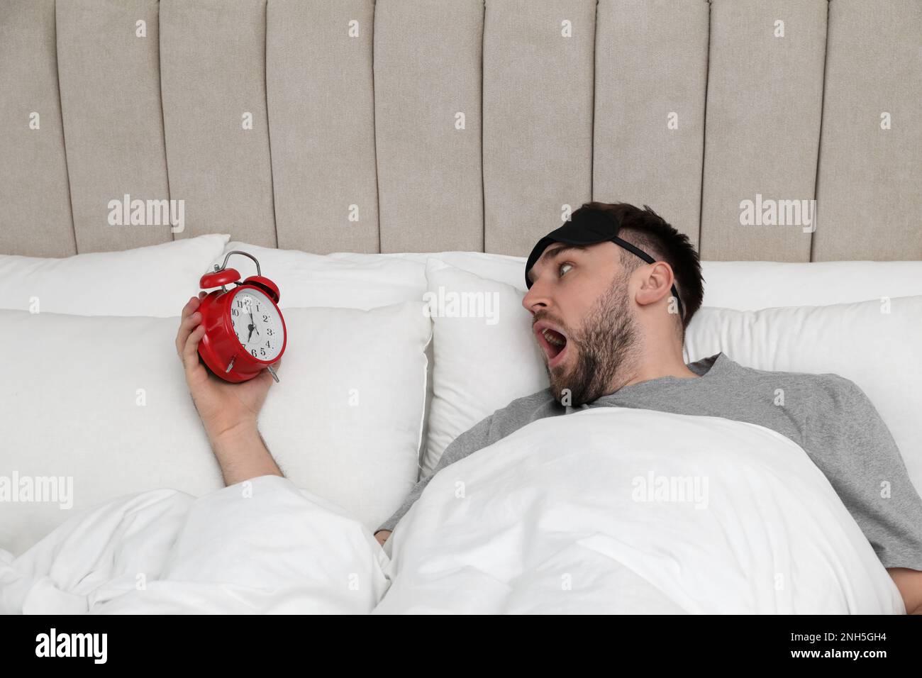 Emotional overslept man with alarm clock in bed, above view. Being late ...