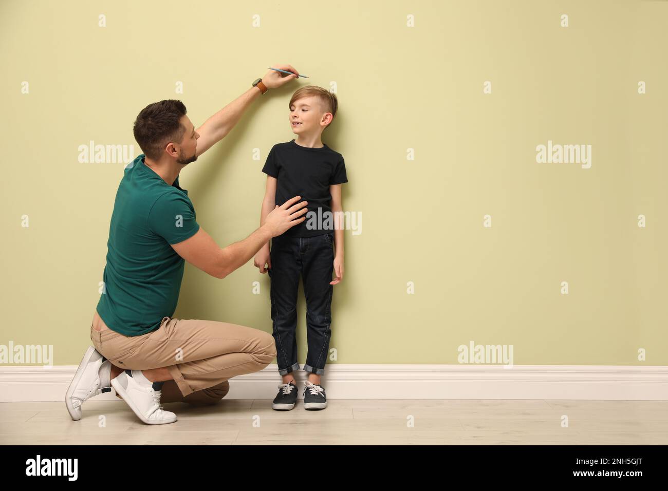 Father measuring height of his son near light wall indoors. Space for ...