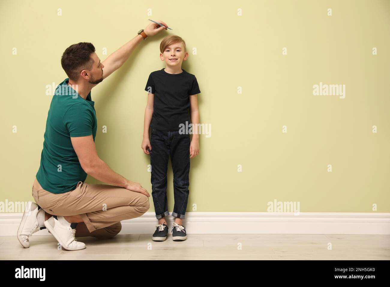 Father measuring height of his son near light wall indoors. Space for ...