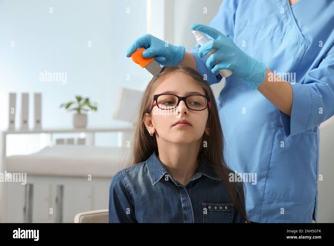 Doctor using nit comb and spray on girl's hair in clinic. Anti lice ...
