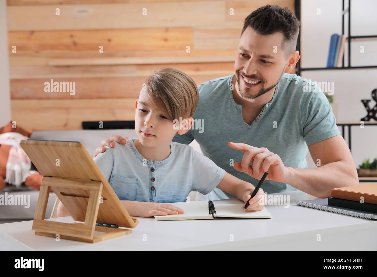Boy with father doing homework using tablet at table in living room ...