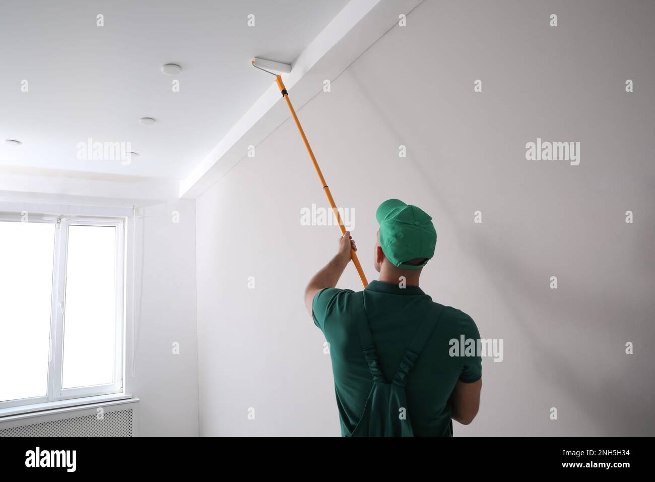 Man painting ceiling with roller in room, back view Stock Photo - Alamy