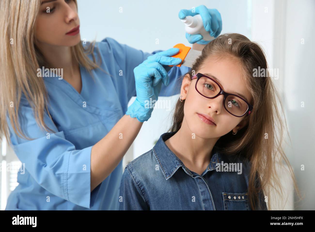 Doctor using nit comb and spray on girl's hair indoors. Anti lice ...