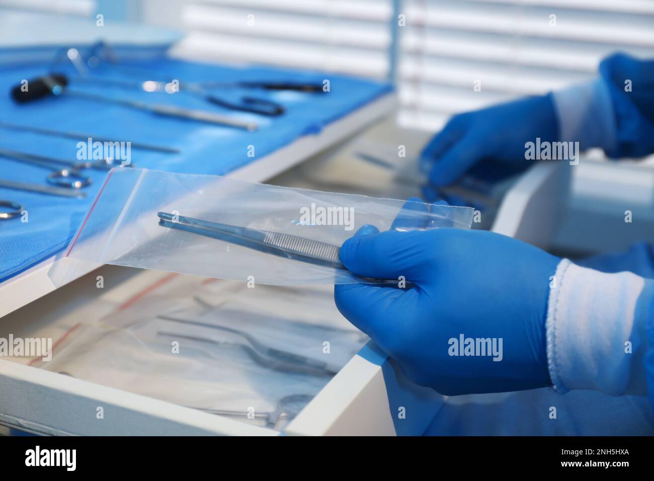 Doctor putting medical forceps into drawer indoors, closeup. Table with ...