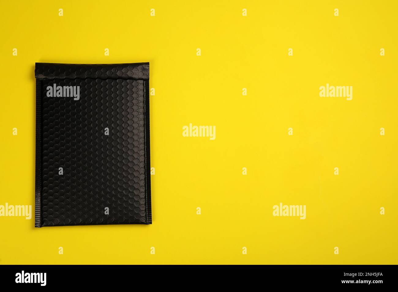 Padded envelope with bubble wrap on yellow background, top view. Space ...