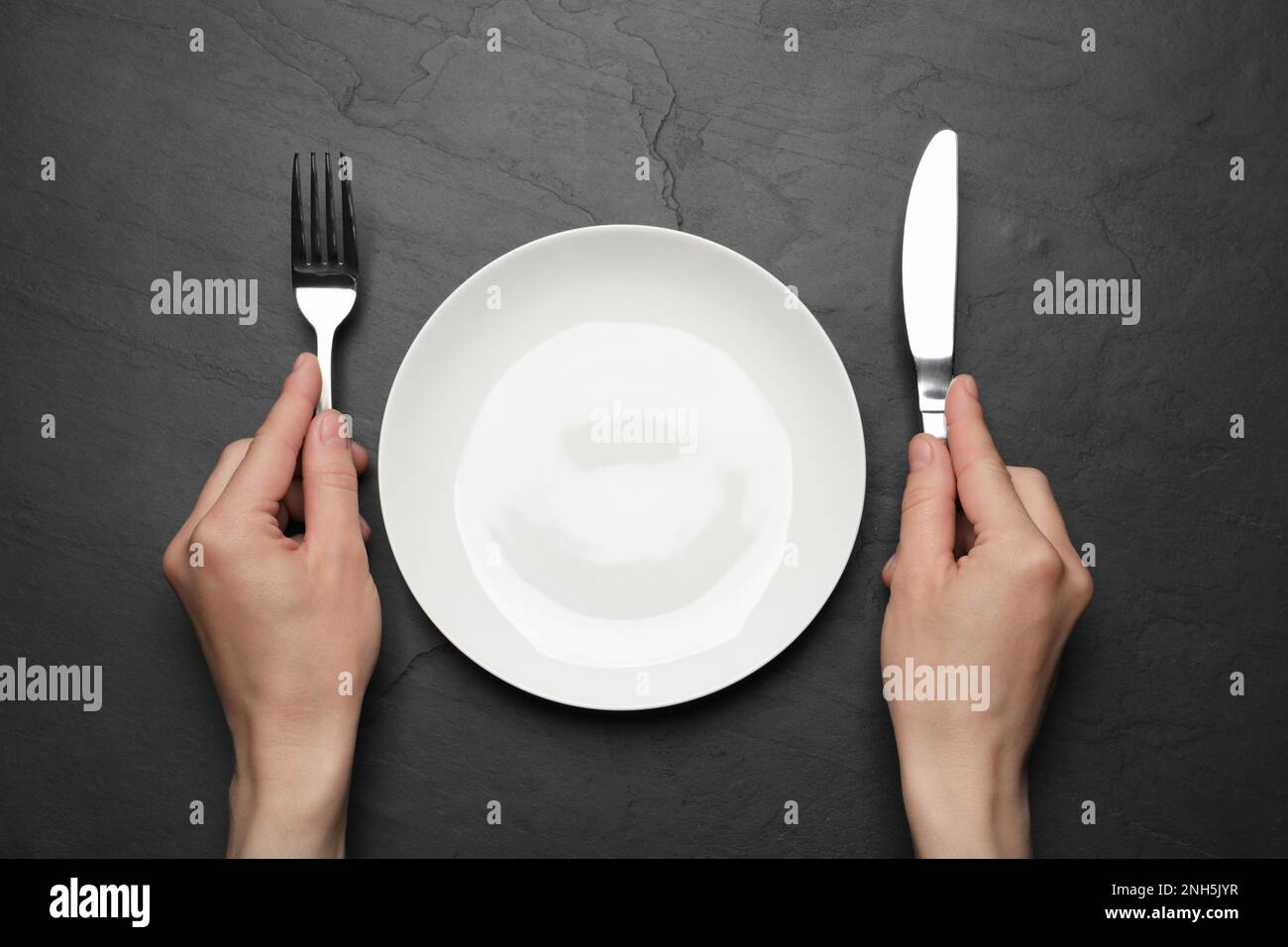 Woman with empty plate and cutlery at black table, top view Stock Photo ...