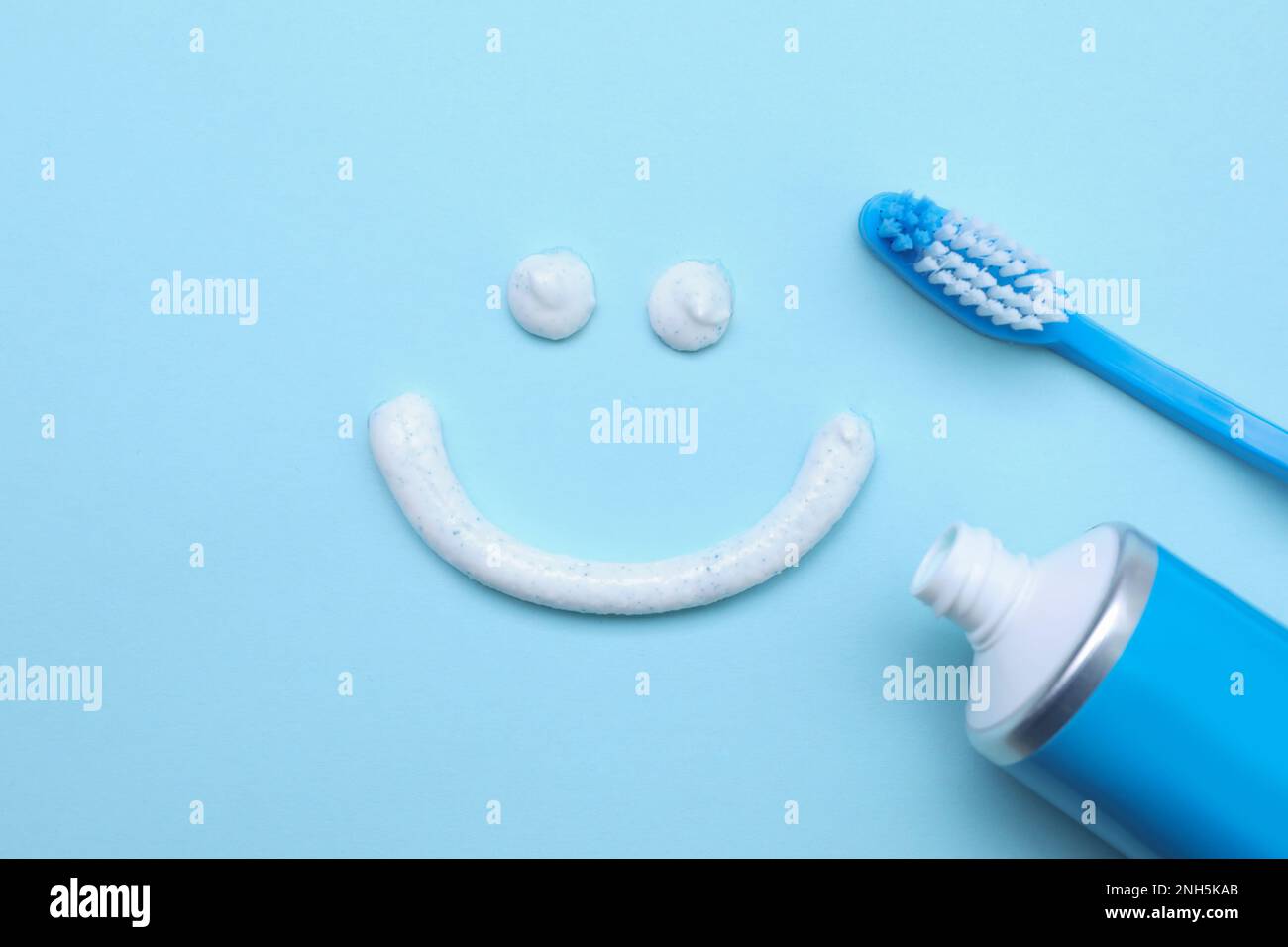 Funny face made with toothpaste, brush and tube on light blue ...