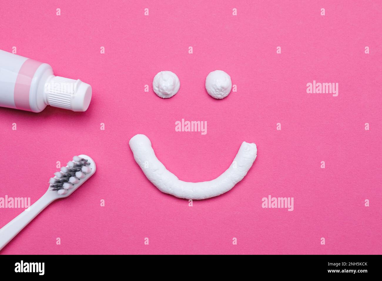 Funny face made with toothpaste, brush and tube on pink background ...