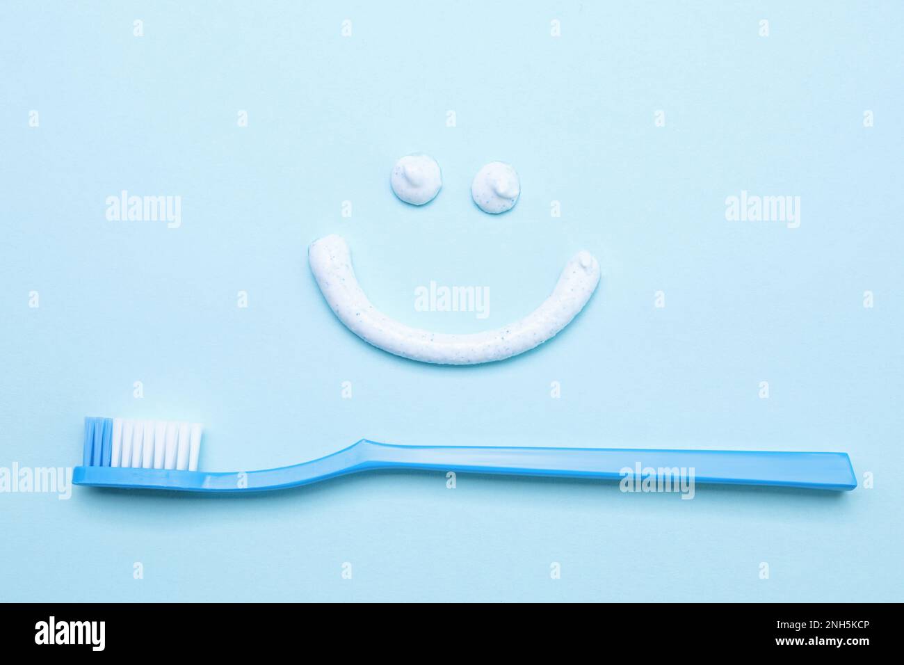 Funny face made with toothpaste and brush on light blue background ...