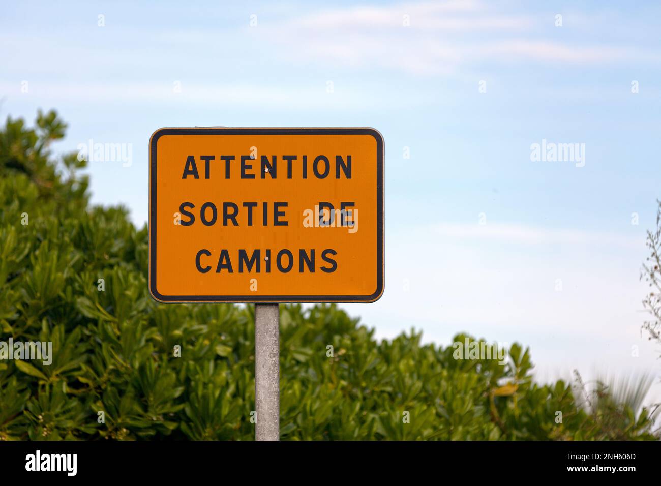 Orange road sign stating in french "Attention sortie de camions ...