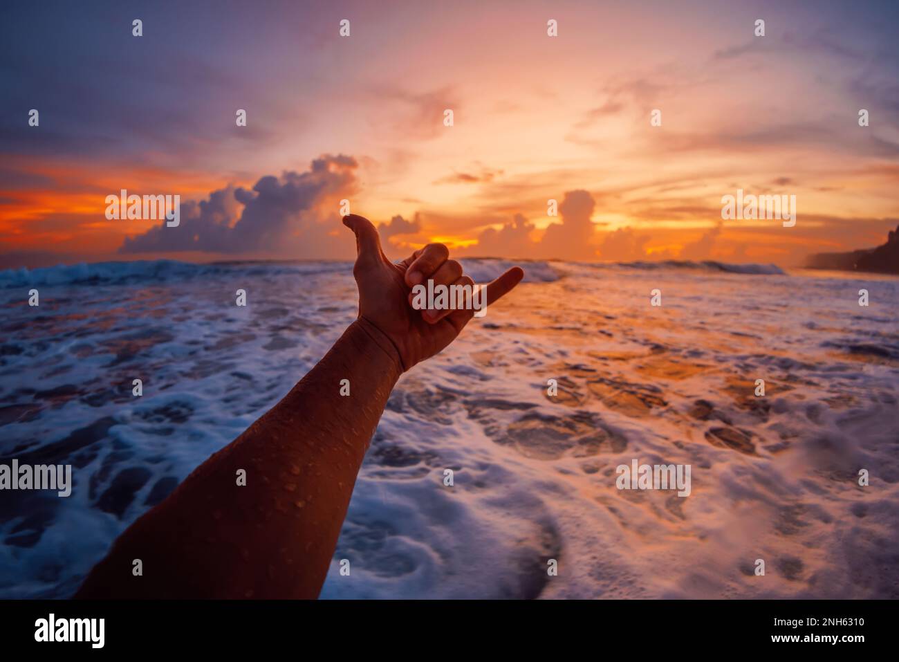 Hand with shaka symbol and waves with colorful sunset in ocean ...