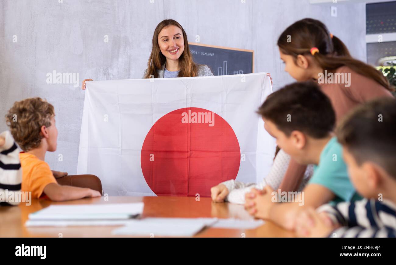 Joyful young woman teacher demonstrating flag for Japan schoolkids ...