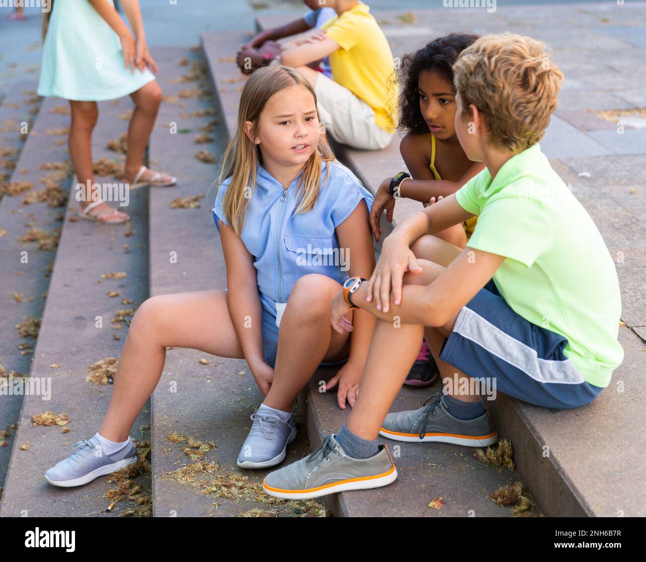 Positive tweenagers friendly blabbing while sitting on steps outdoors ...