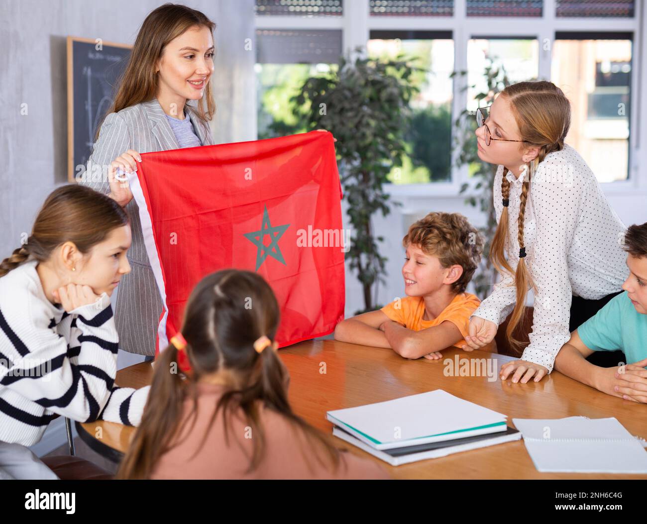 Group of curious preteen learners and young female teacher with flag of ...