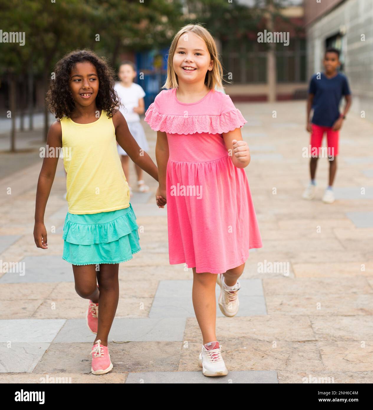 Two cheerful preteen girls enjoying walk along city street in summer ...