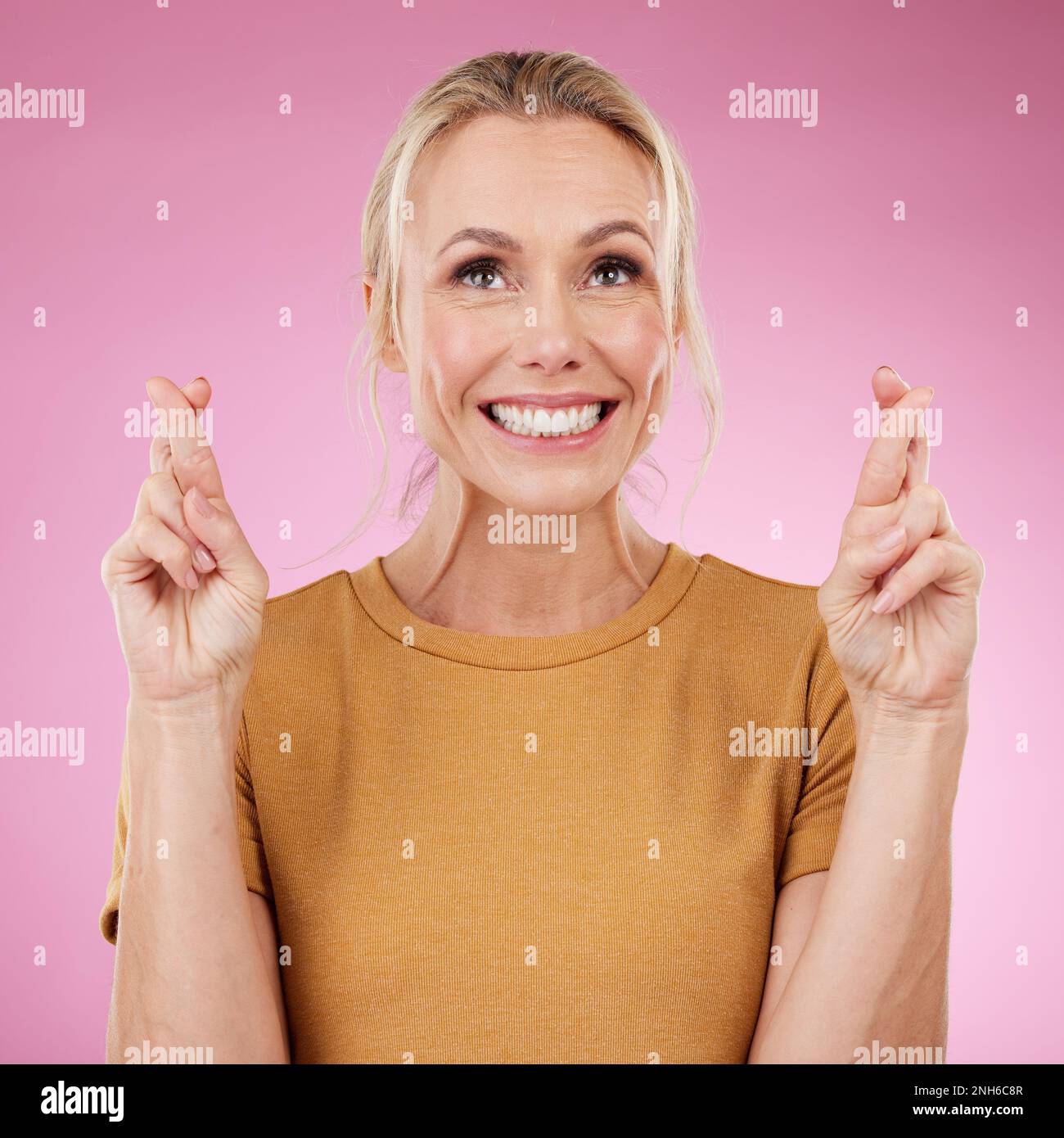 Woman, fingers crossed and smile in studio, pink background and good ...