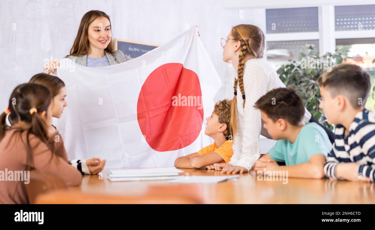 Joyful young woman teacher demonstrating flag for Japan schoolkids ...