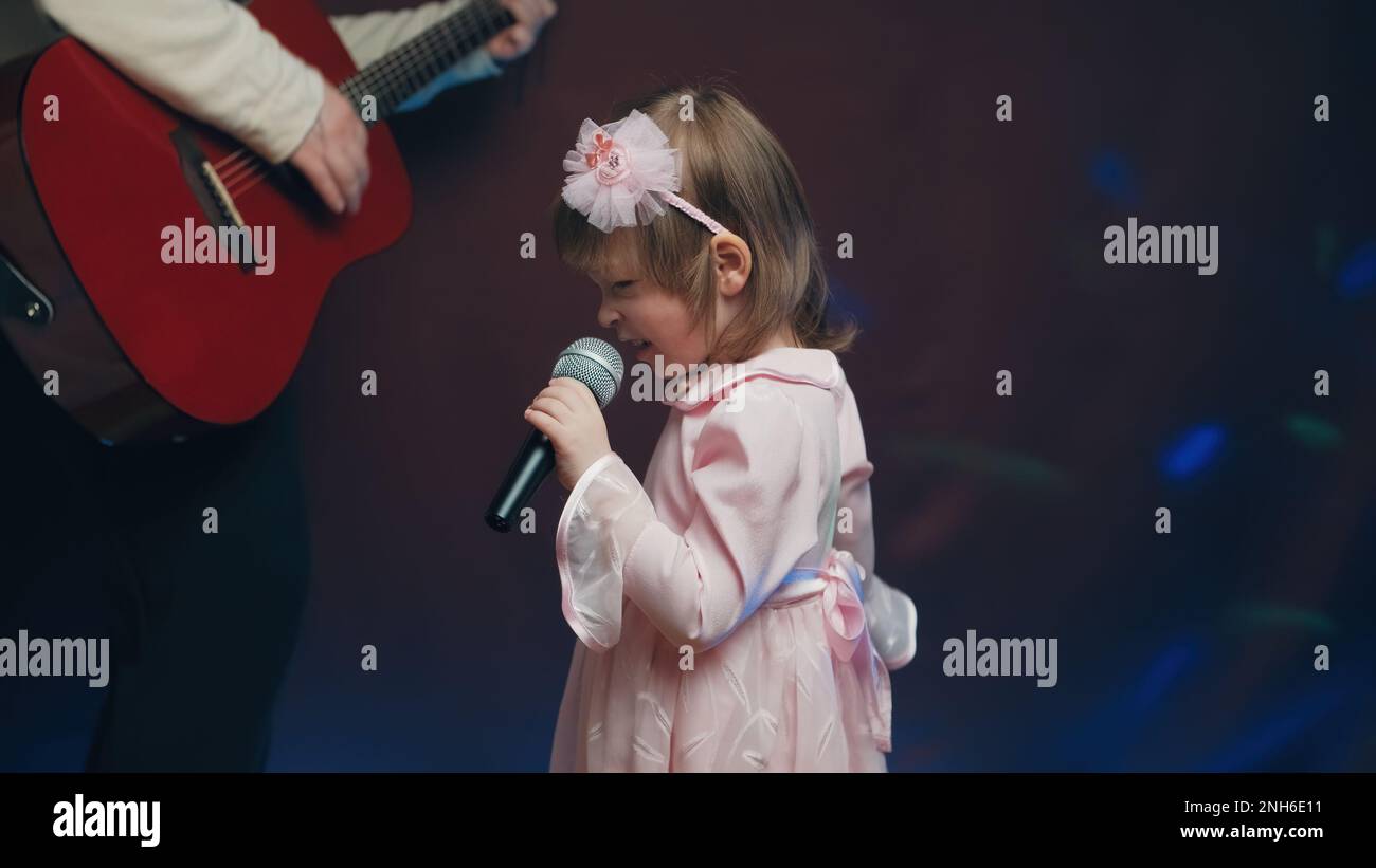 Llittle girl in vintage dress sings on stage, her father plays acoustic ...