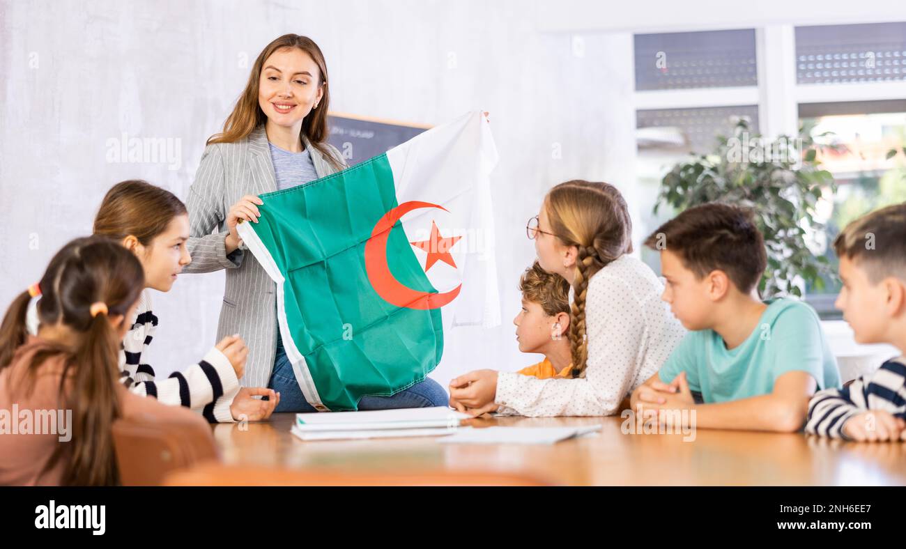 Smiling young woman teacher showing state flag of Algeria and telling ...