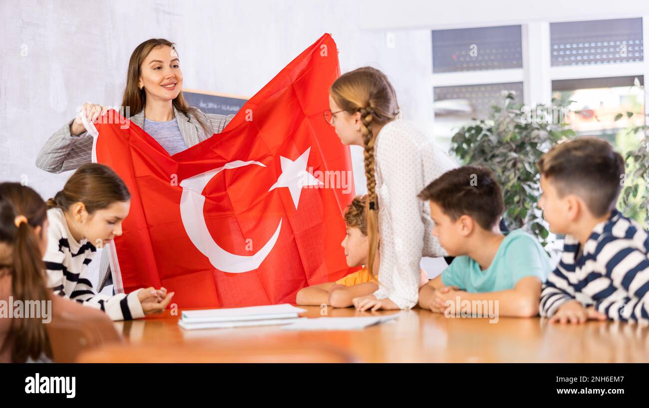 Cheerful young woman teacher demonstrating Turkish flag for schoolkids ...