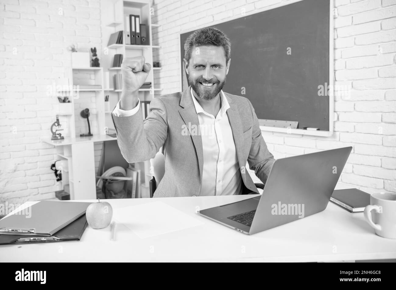 successful school teacher in classroom with computer at blackboard ...