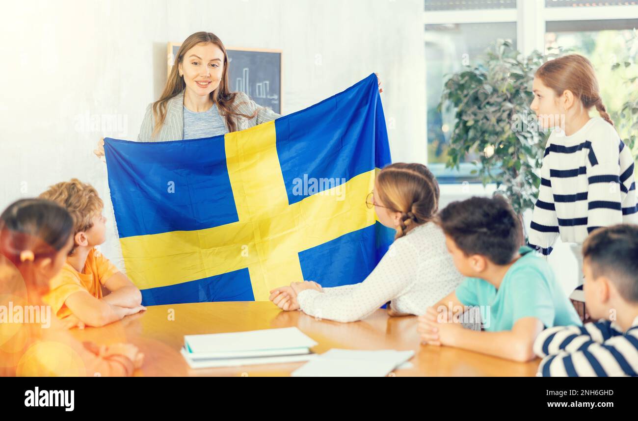 Group of curious preteen learners and young female teacher with flag of ...